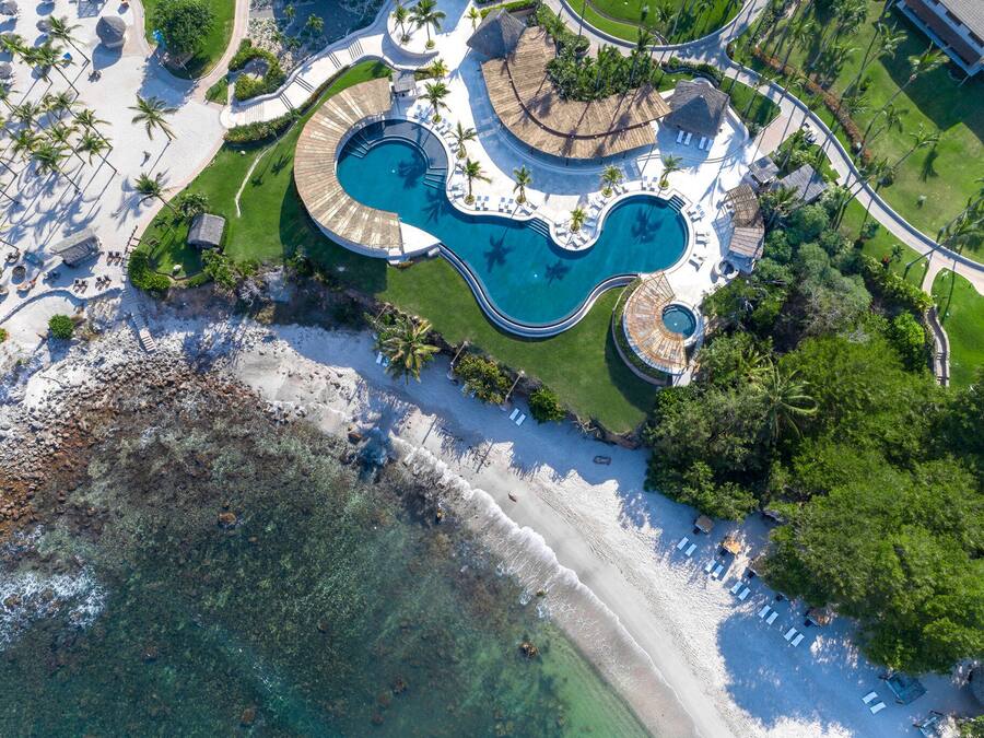 Vista aérea de um resort com uma grande piscina, praia e palmeiras.