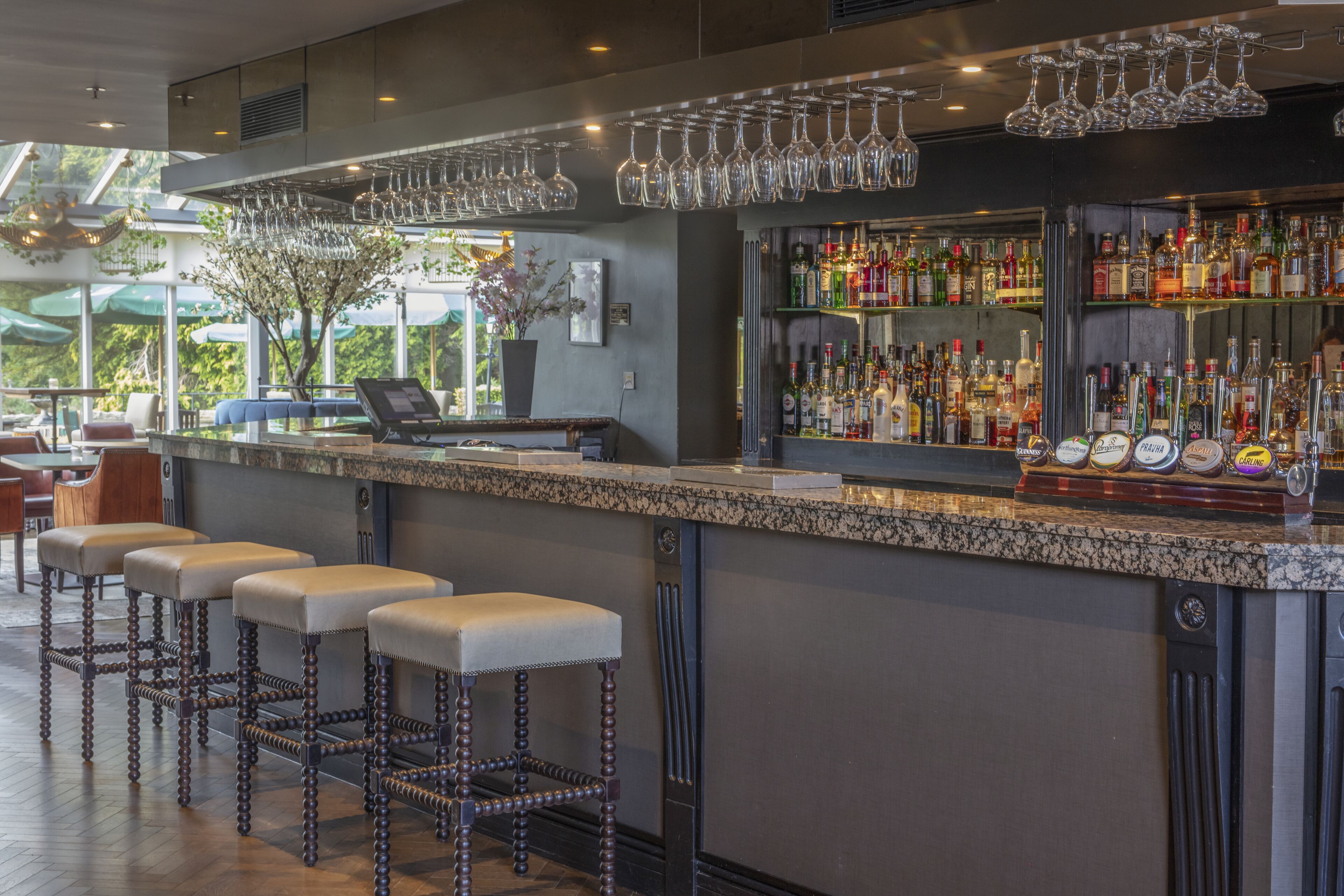 Uma área de bar com bancada de granito, banquetas e diversos tipos de bebidas alcoólicas.