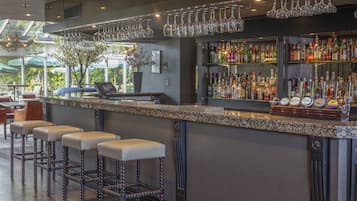 Uma área de bar com bancada de granito, banquetas e diversos tipos de bebidas alcoólicas.