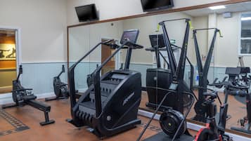 Ginásio com máquinas de cardio, um espelho e uma televisão.