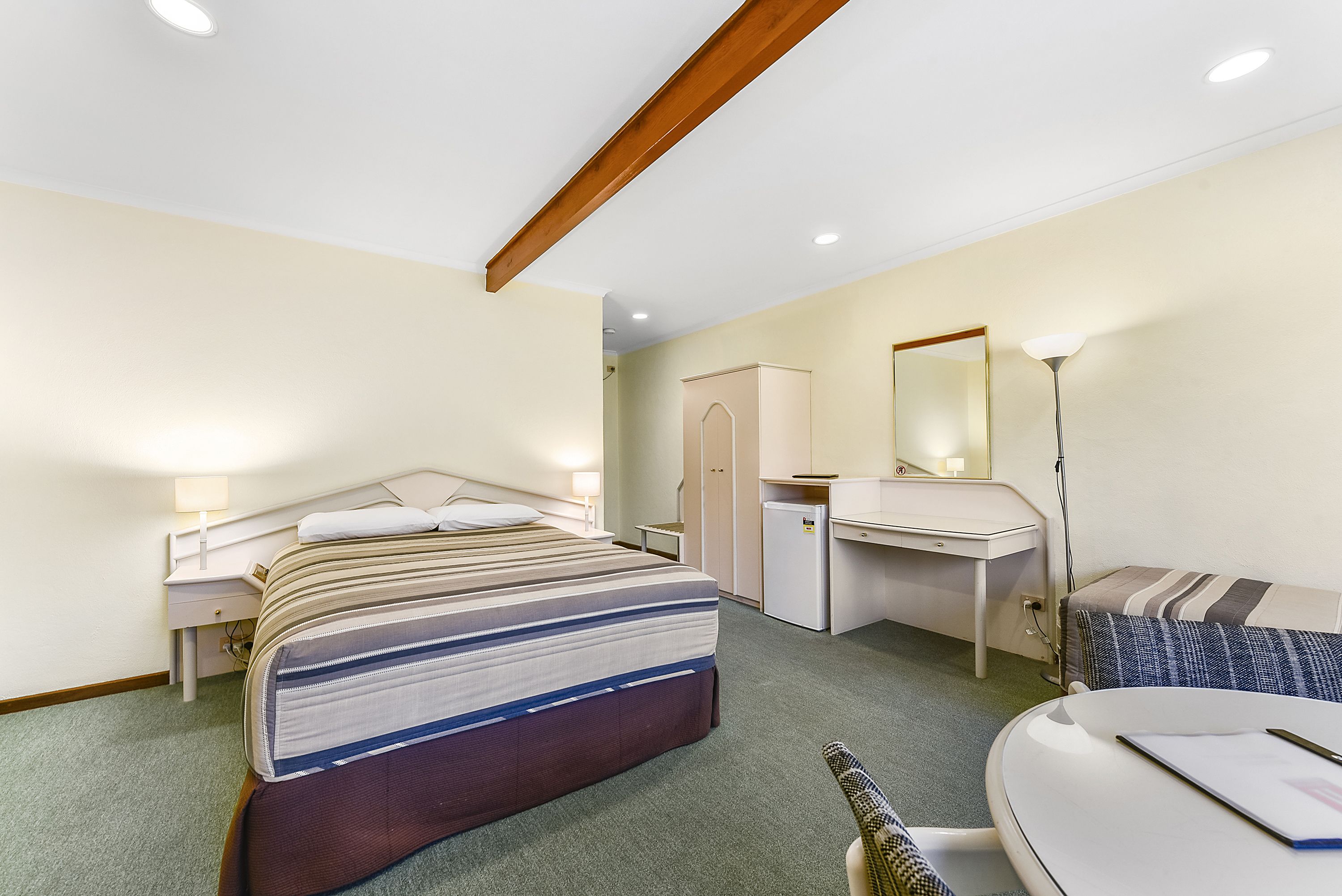 Quarto de hotel com cama, escrivaninha, cadeira, guarda-roupa e espelho.