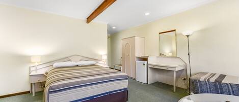 Quarto de hotel com cama, escrivaninha, cadeira, guarda-roupa e espelho.