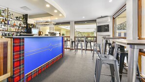 Uma área de bar com balcão azul, prateleiras com garrafas e uma televisão.