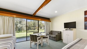 Quarto de hotel com uma grande janela, uma mesa de jantar com cadeiras, um sofá, uma televisão sobre um móvel e uma cama.
