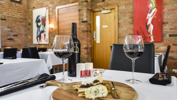 Uma mesa de jantar posta com taças de vinho, uma garrafa, queijo e uma vela.