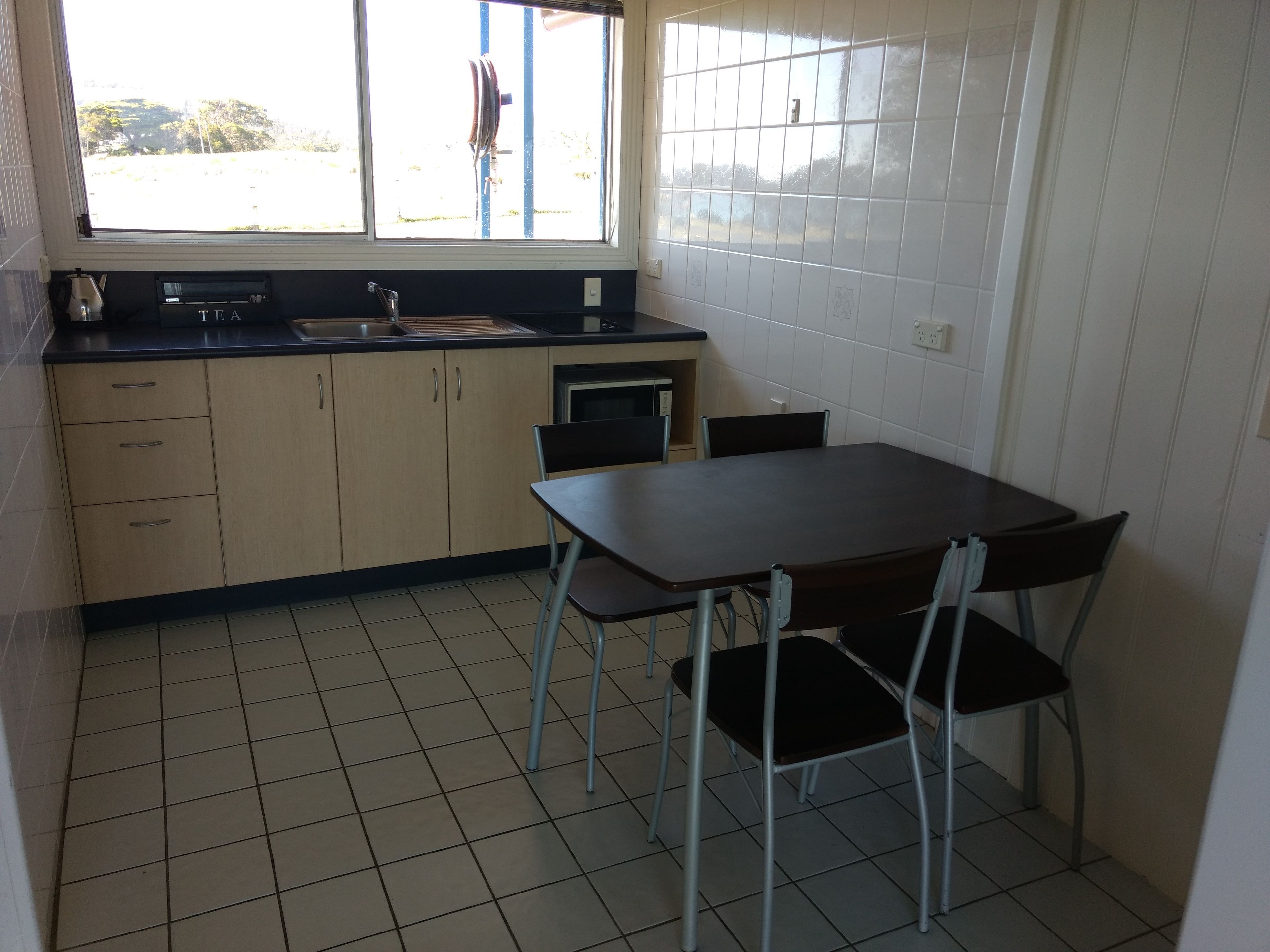 Uma cozinha pequena com janela, pia, fogão e uma mesa com cadeiras.