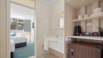 Quarto de hotel com cama, banheiro com pia e cafeteira.