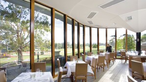 Um restaurante com amplas janelas, mesas preparadas para refeições e vista para o exterior.