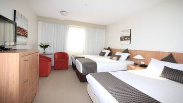 Quarto de hotel com duas camas, uma escrivaninha, uma TV e uma cadeira vermelha.