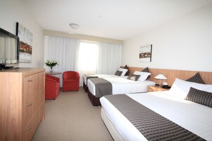 Quarto de hotel com duas camas, uma escrivaninha, uma TV e uma cadeira vermelha.
