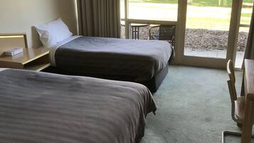 Quarto de hotel com duas camas, janela com vista para um parque e uma pequena mesa com uma cadeira.