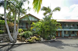 Um edifício de dois andares com varanda no andar superior, cercado por vegetação tropical.