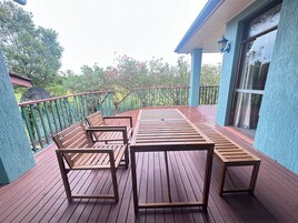 Um deck de madeira com mesa e cadeiras, guarda-corpo e vista para o verde.