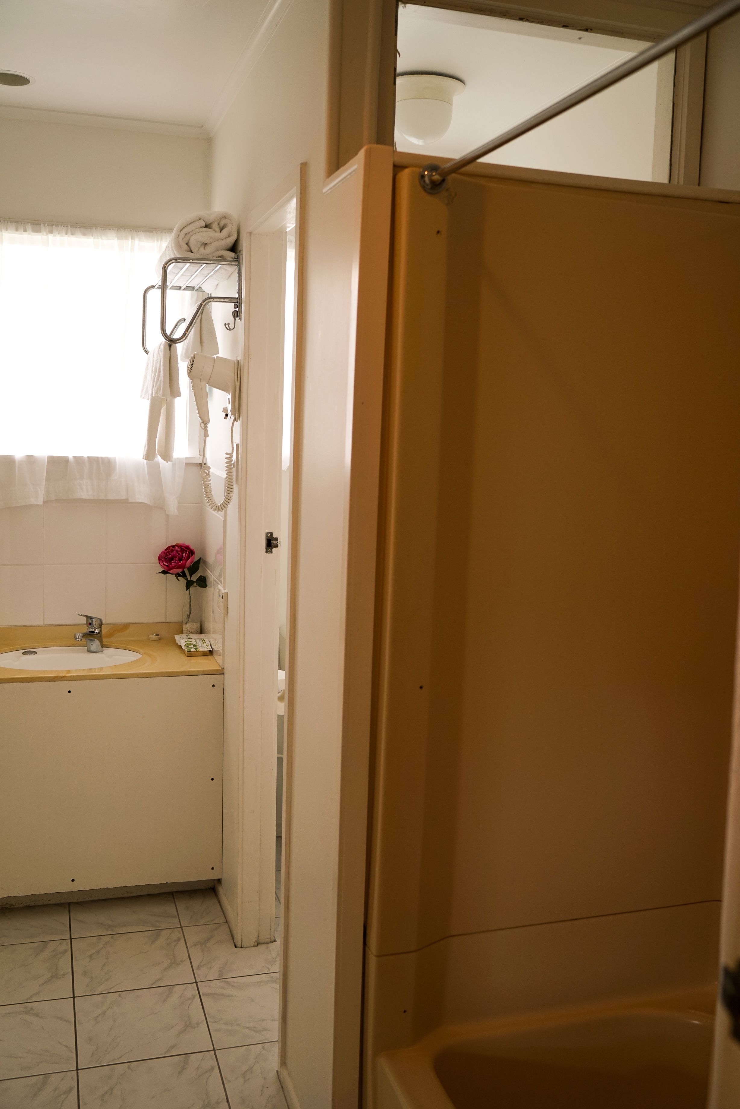 Casa de banho com chuveiro, lavatório com espelho e um porta-toalhas.