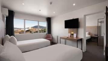Quarto de hotel com duas camas, escrivaninha, televisão e vista para o exterior.