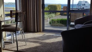 Uma sala de estar moderna com uma grande porta de vidro deslizante que dá para uma varanda com vista para o mar e uma van estacionada.