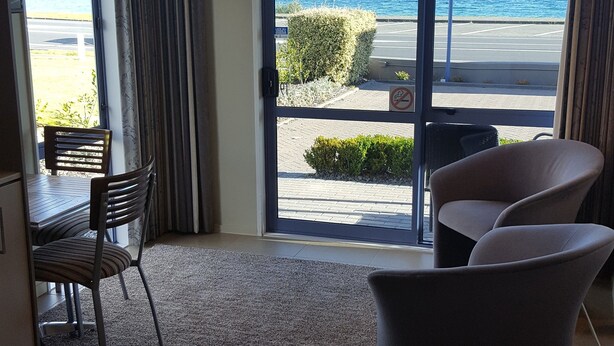 Quarto com mesa de jantar e cadeiras, um sofá, uma ampla porta de vidro deslizante com vista para o mar e um lustre no teto.
