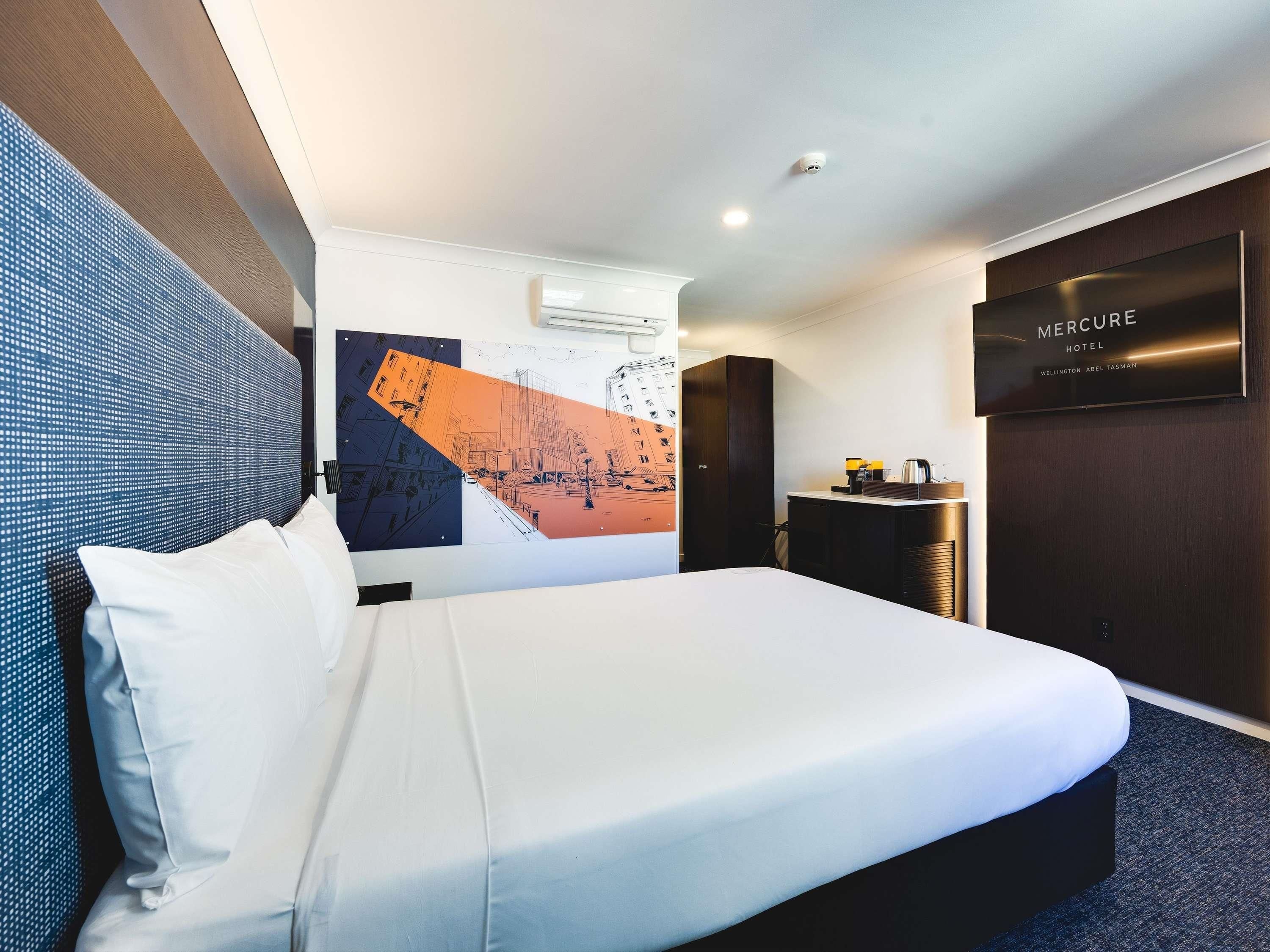 Quarto de hotel com cama grande, escrivaninha, guarda-roupa e placa na parede.