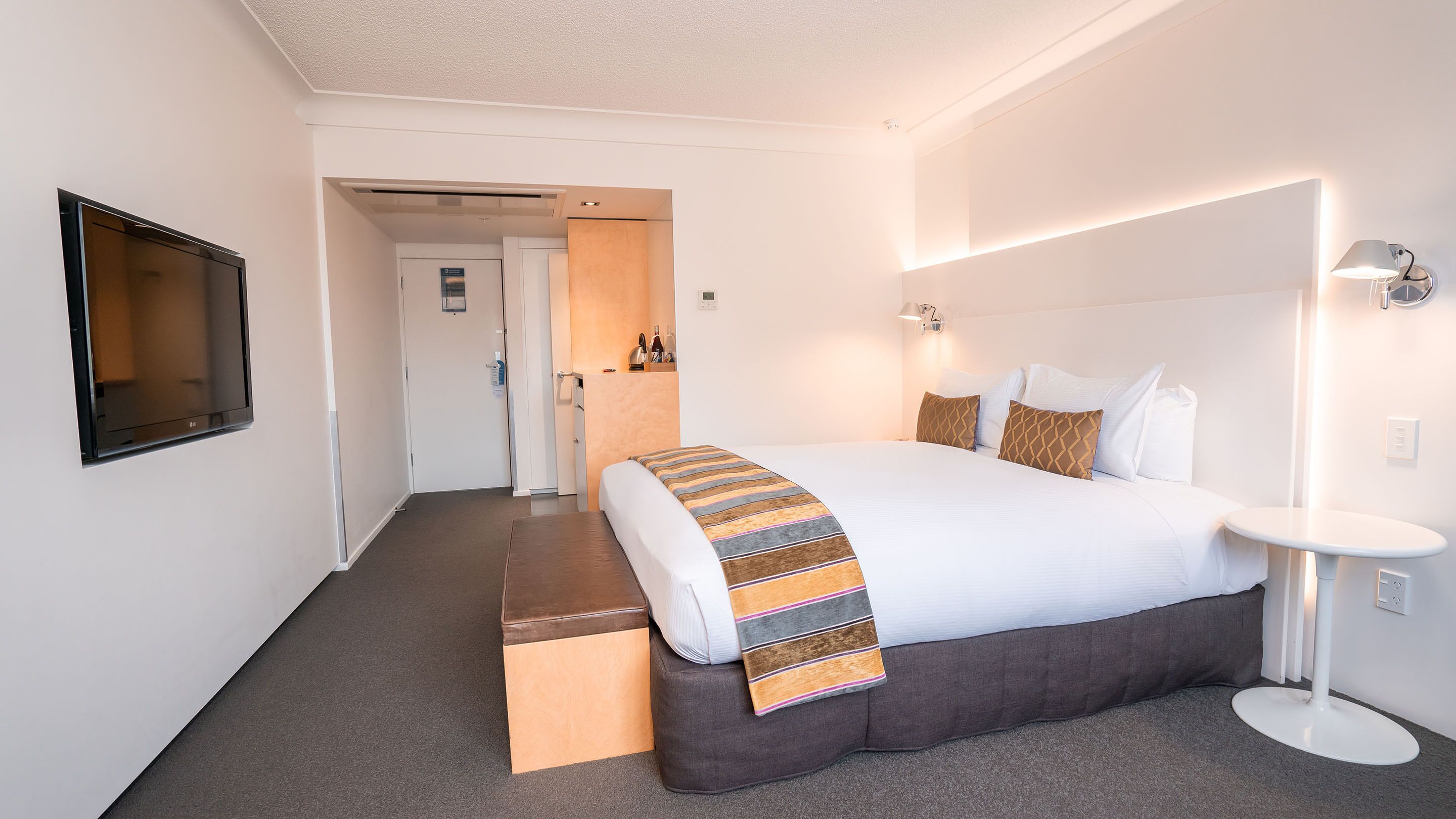 Quarto de hotel com cama grande, mesa de cabeceira, televisão de tela plana na parede e porta para o banheiro.