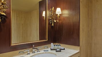 Casa de banho com um espelho grande, lavatório e toucador com artigos de higiene pessoal.