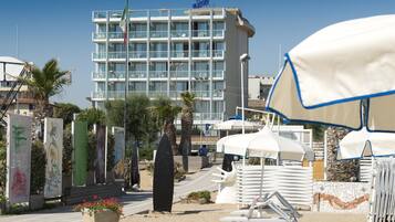 Um hotel com fachada de vidro moderna, uma bandeira e guarda-sóis de praia.