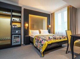 Quarto de hotel com cama, escrivaninha, guarda-roupa e minibar.