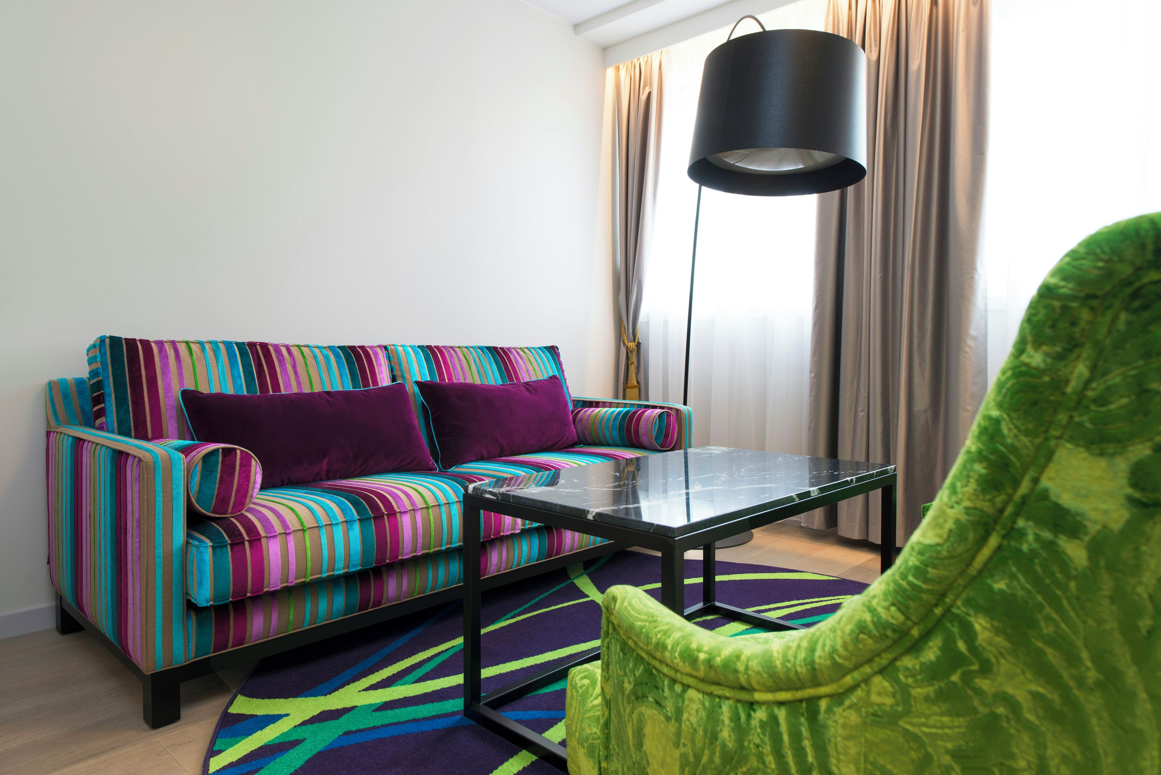 Uma sala de estar moderna com um sofá colorido listrado, uma mesa de centro de vidro e uma poltrona verde.