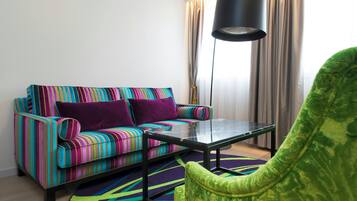 Uma sala de estar moderna com um sofá colorido listrado, uma mesa de centro de vidro e uma poltrona verde.