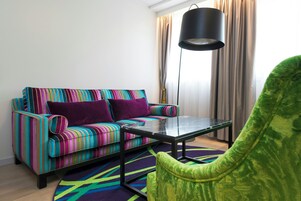 Uma sala de estar moderna com um sofá colorido listrado, uma mesa de centro de vidro e uma poltrona verde.