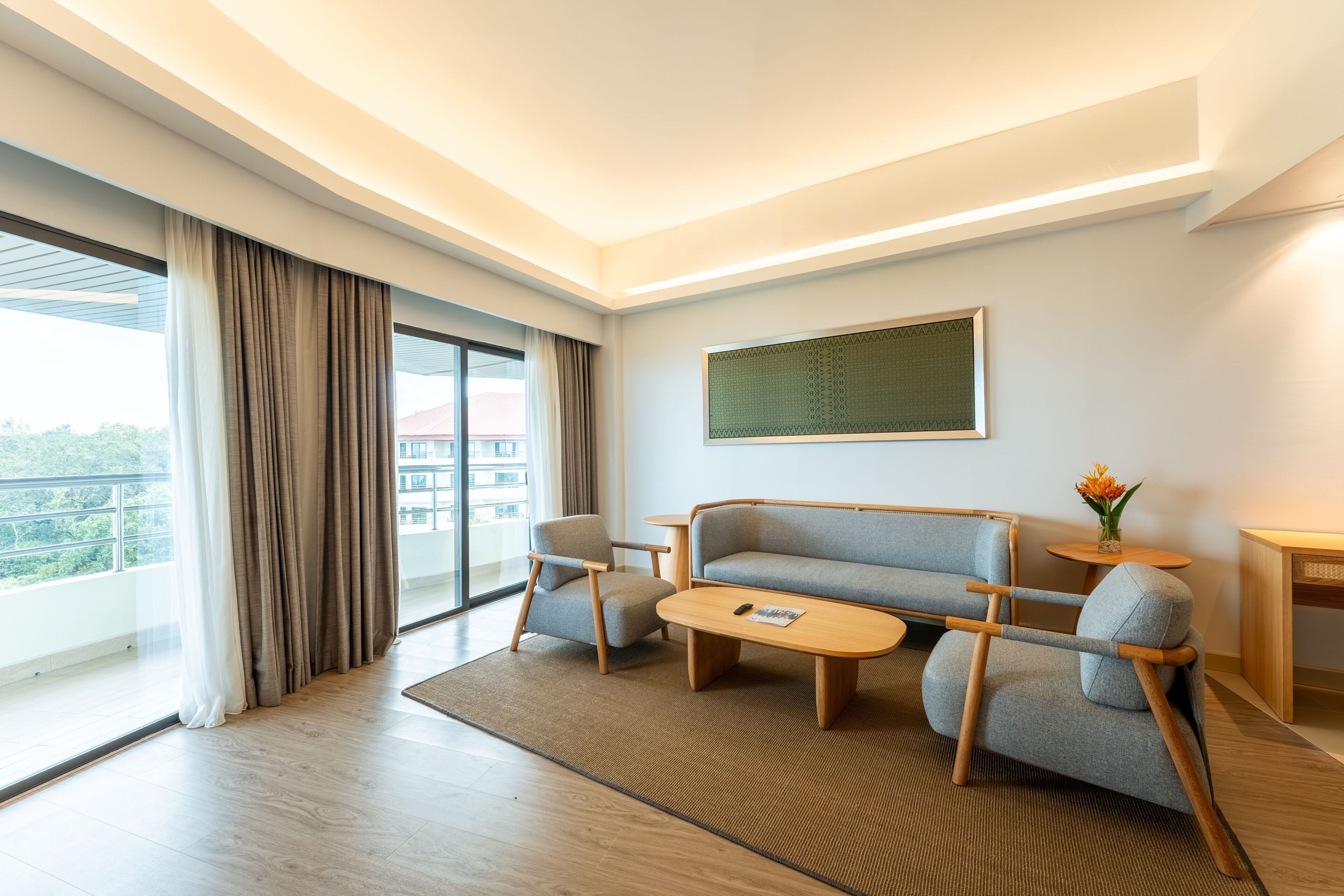Quarto de hotel moderno com sofá, duas poltronas, mesa de centro e uma mesinha de apoio.