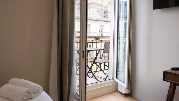 Quarto de hotel com porta de vidro deslizante para uma varanda externa, com mesa e cadeiras.