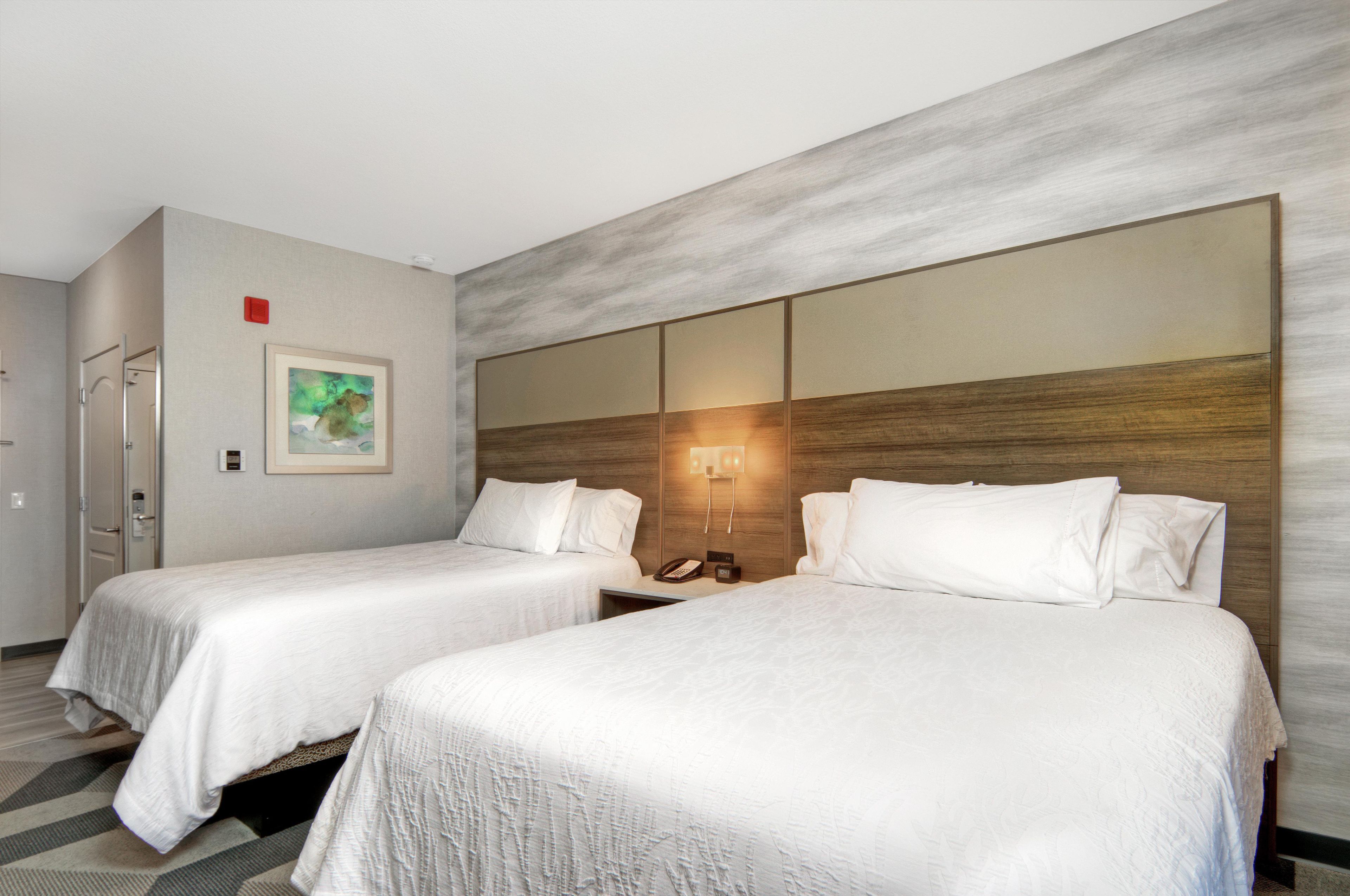 Quarto de hotel com duas camas, um quadro na parede e uma cabeceira de madeira.