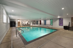 Piscina interior com água cristalina, rodeada por piso e paredes revestidas de azulejos.