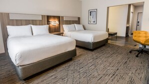Quarto de hotel com duas camas, uma escrivaninha, uma cadeira e uma luminária fixada na parede.