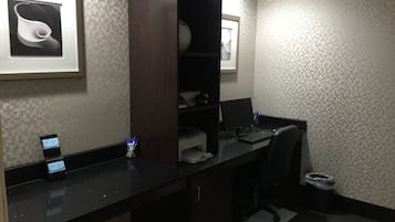 Quarto de hotel com escrivaninha, computador, cadeira e uma moldura na parede.