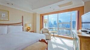 Quarto de hotel com uma cama grande, uma cadeira, uma mesa de escritório com televisão e uma janela ampla com vista para a cidade.