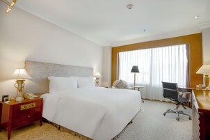 Quarto de hotel com cama grande, abajures, escrivaninha com cadeira e janela com cortinas.
