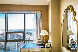 Quarto de hotel com uma janela grande, uma escrivaninha com abajur, telefone e espelho.
