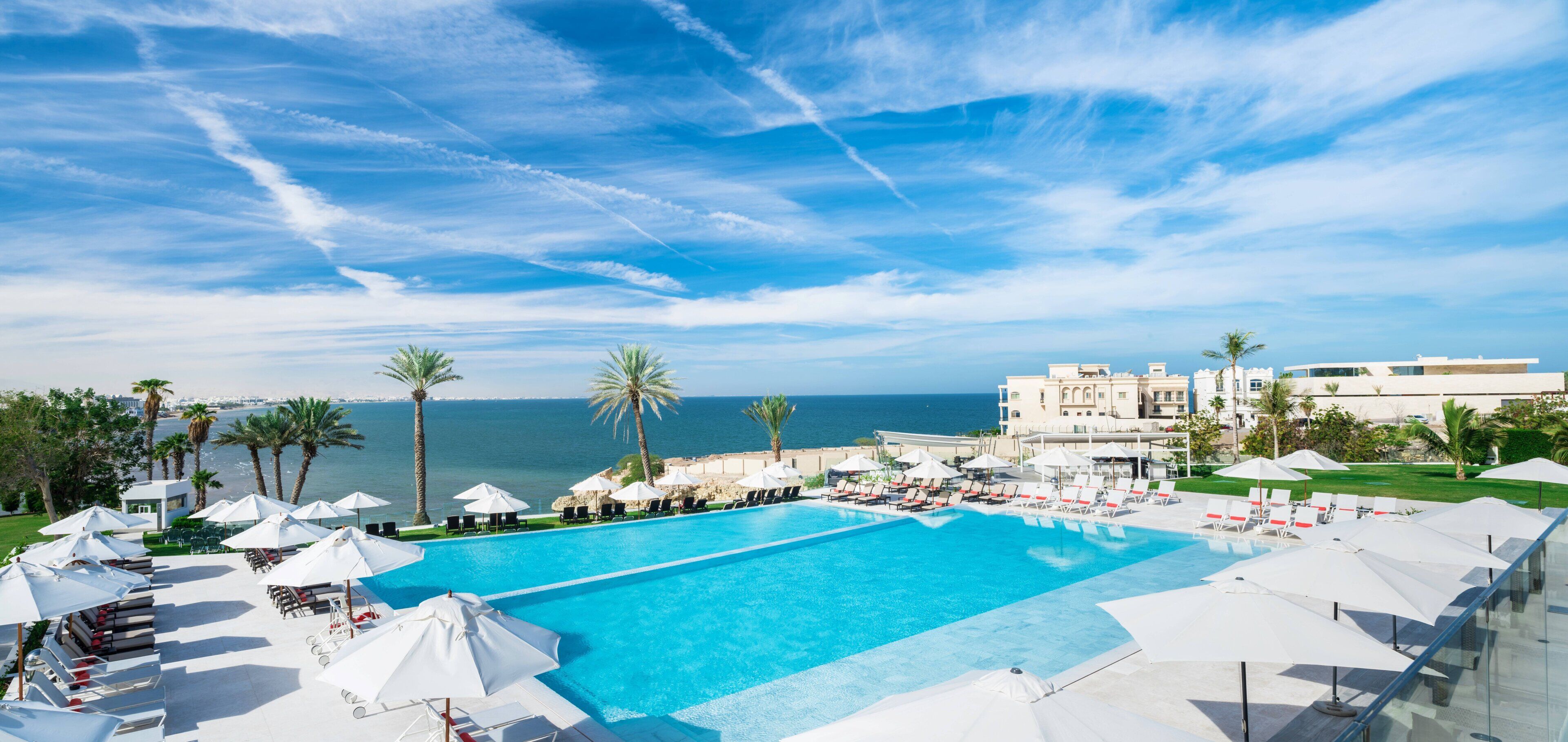 Área da piscina com espreguiçadeiras e guarda-sóis, céu limpo e vista para o mar.