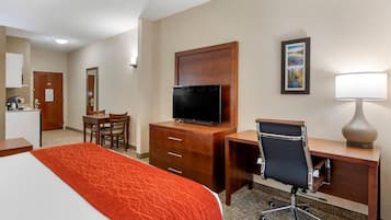 Quarto de hotel com cama, escrivaninha, cadeira, televisão, luminária e quadro pendurado na parede.