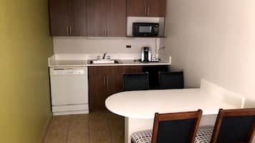 Cozinha compacta equipada com micro-ondas, cafeteira e máquina de lavar loiça. Inclui uma mesa de jantar com duas cadeiras.