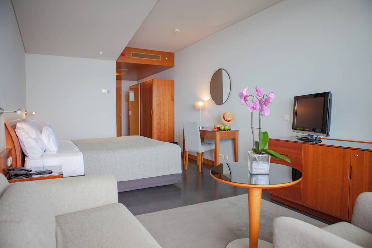 Quarto de hotel moderno com cama, escrivaninha, televisão e área de estar.