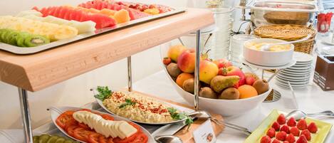 Buffet com diversas opções de comida, incluindo frutas, legumes e uma seleção de queijos.