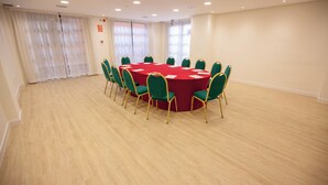 Uma sala de conferências com mesa redonda, cadeiras verdes e toalha de mesa vermelha.