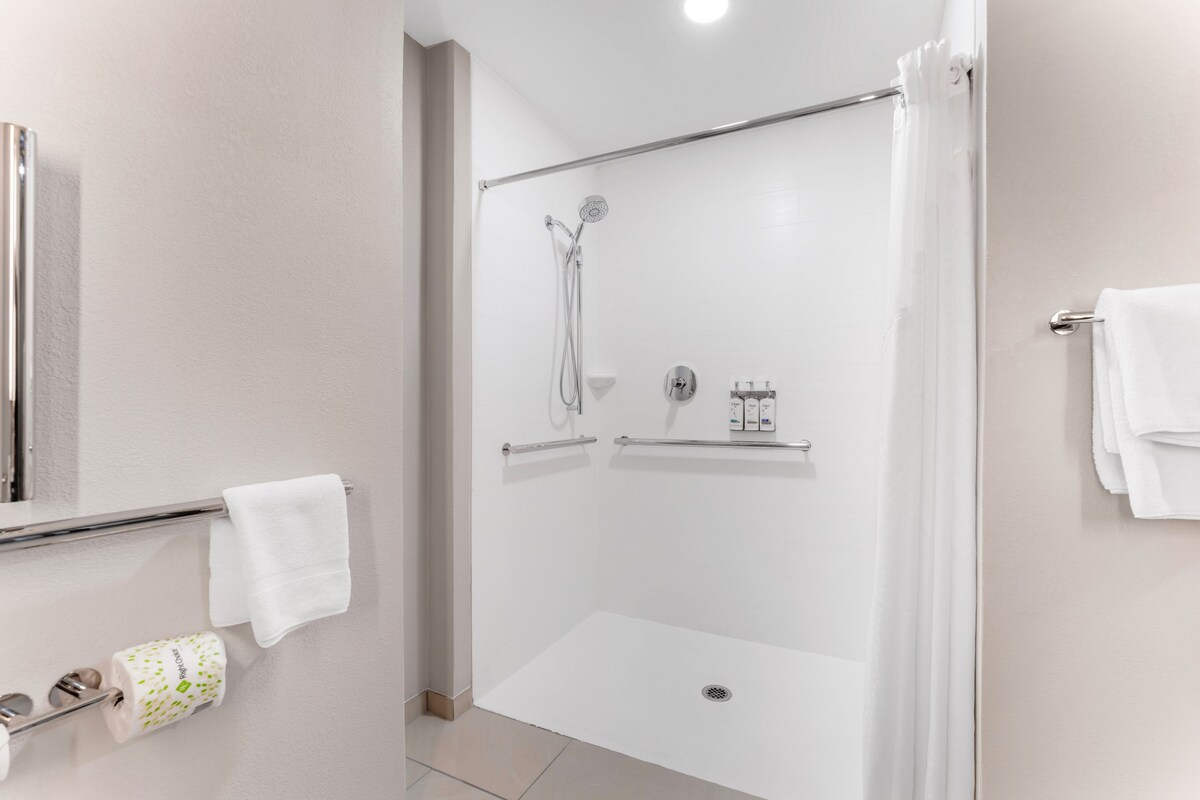 Uma casa de banho moderna com cabine de duche em vidro, suporte de papel higiénico e barra para toalhas.