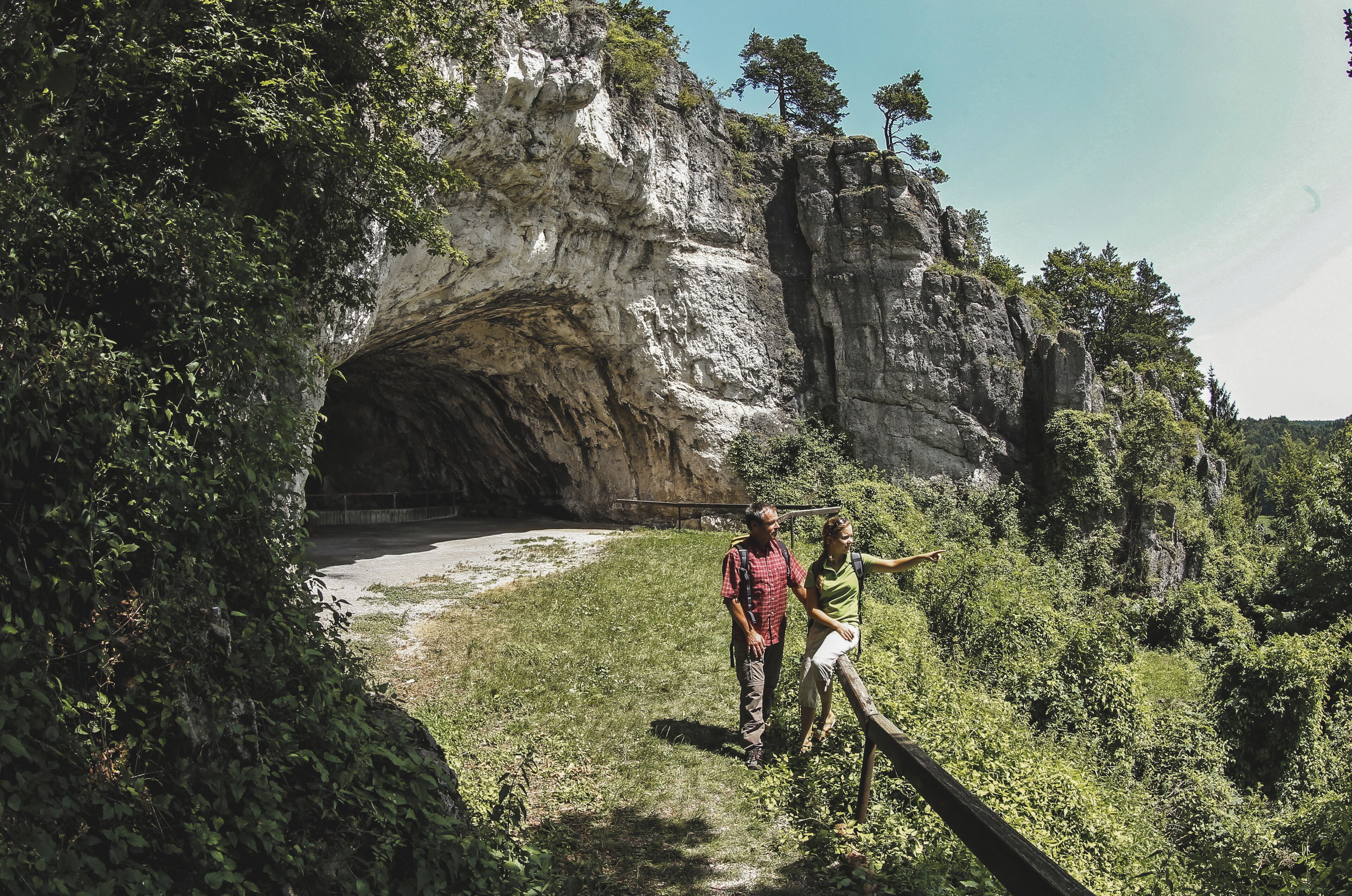 Formação rochosa natural com entrada de caverna, rodeada por vegetação.