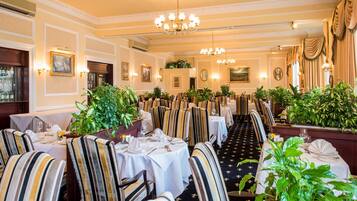 Uma sala de jantar formal com cadeiras listradas, toalhas de mesa brancas e lustres.