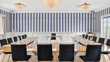 Uma sala de conferências com uma mesa comprida, cadeiras pretas e lustres.