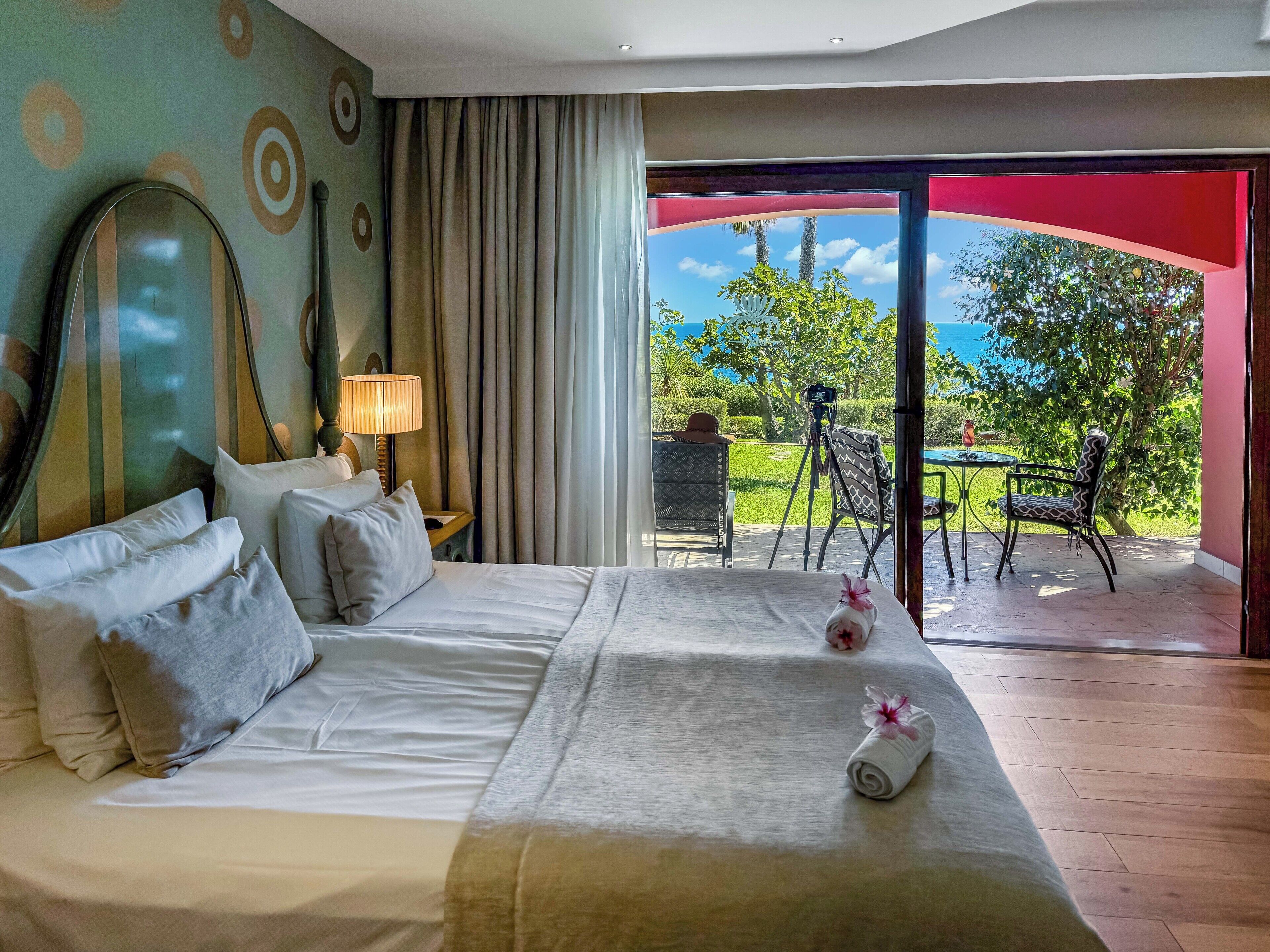 Quarto de hotel com cama, mesa de cabeceira, luminária e vista para o exterior.