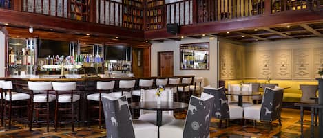 Uma área de bar com teto de madeira, estantes de livros e piso estampado.